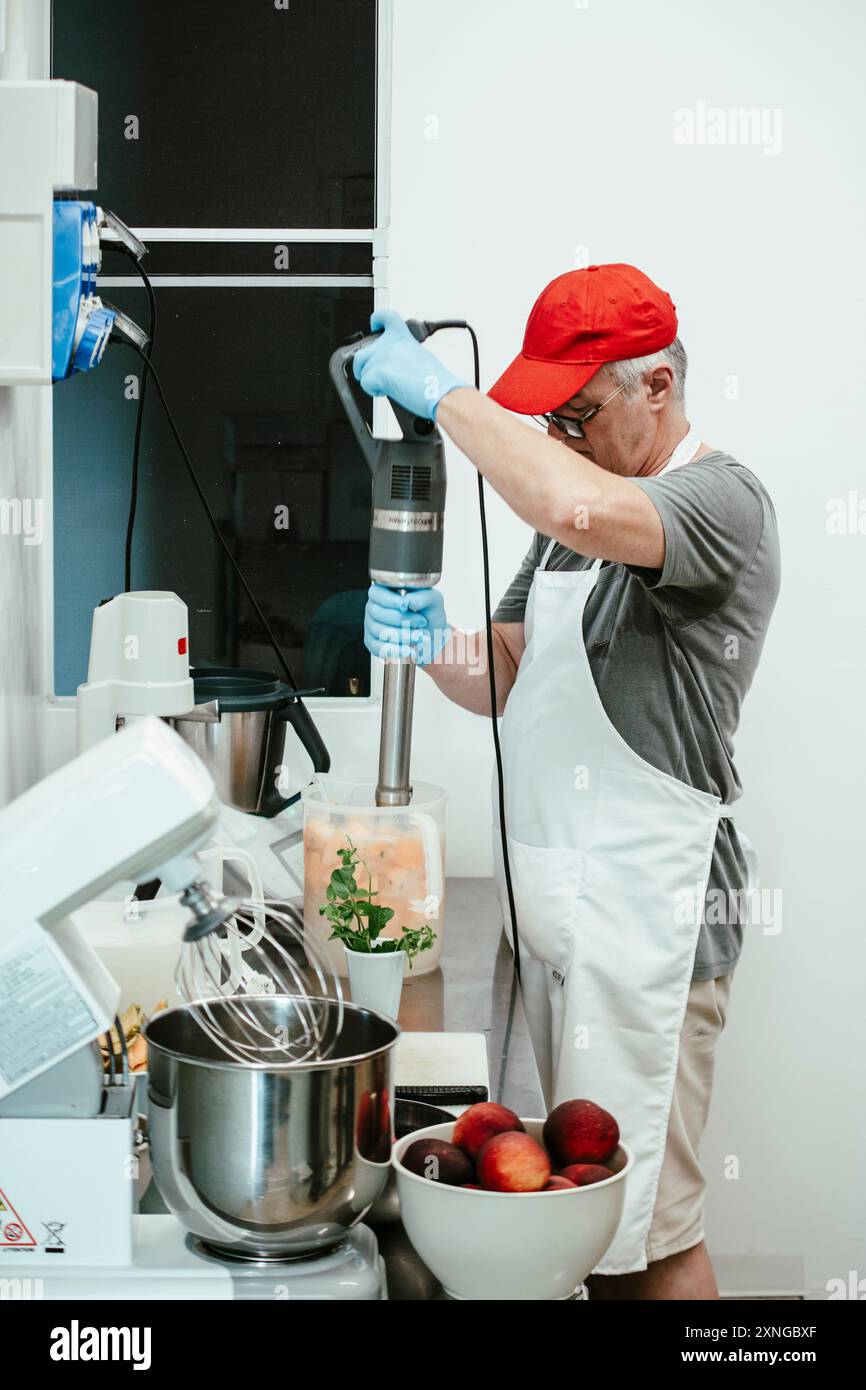 Pastry chef wearing a white apron and a red cap using an immersion ...