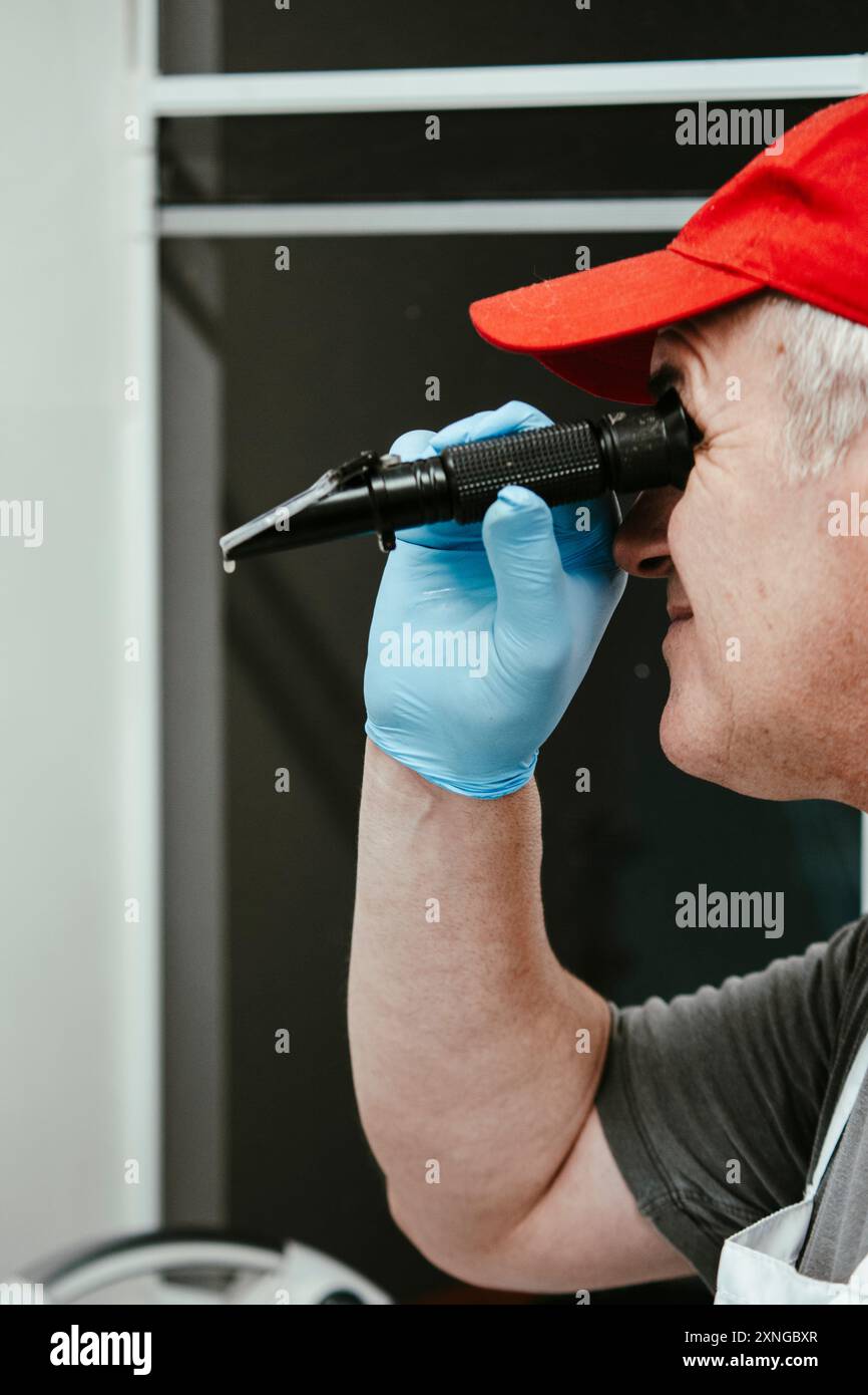 Food scientist in a lab coat and gloves uses a refractometer in a ...