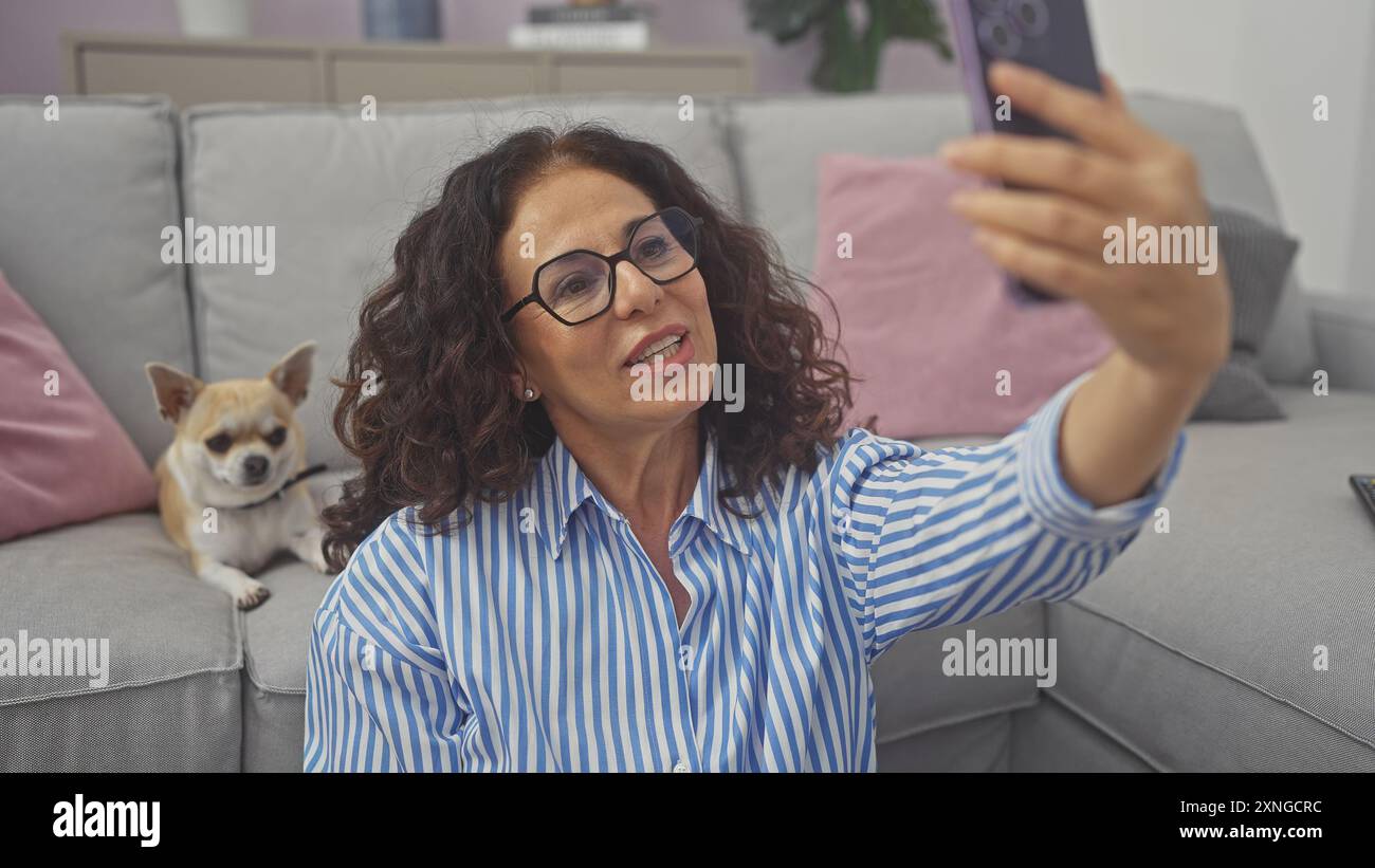A middle-aged hispanic woman takes a selfie with her chihuahua in a cozy living room Stock Photo ...