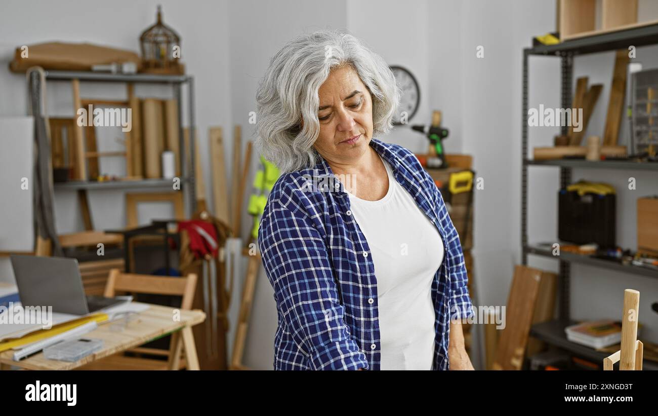 A mature woman with grey hair stands thoughtfully in a cluttered ...