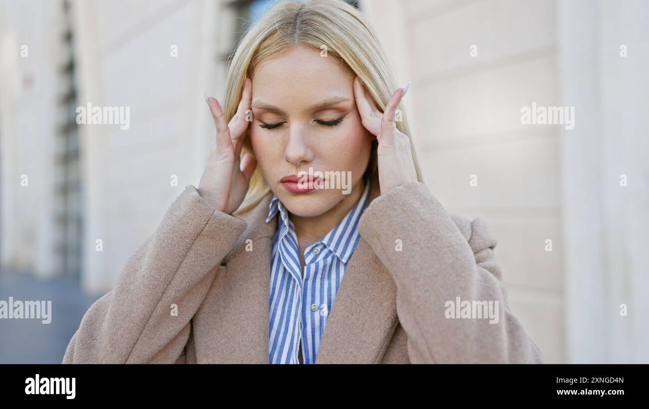 A stressed young woman in a beige coat stands on a city street, her ...