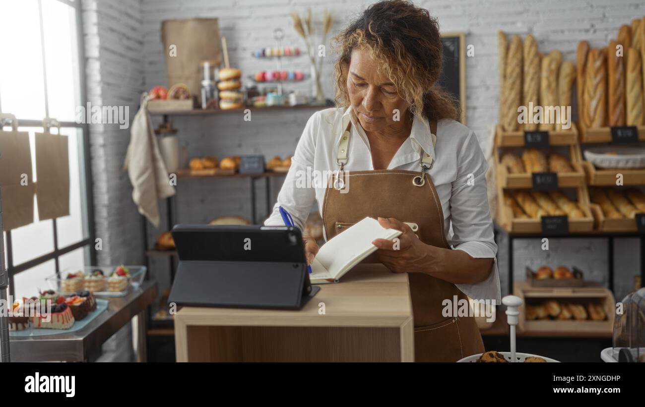 Middle-aged woman in a bakery writing in a notebook while checking a ...
