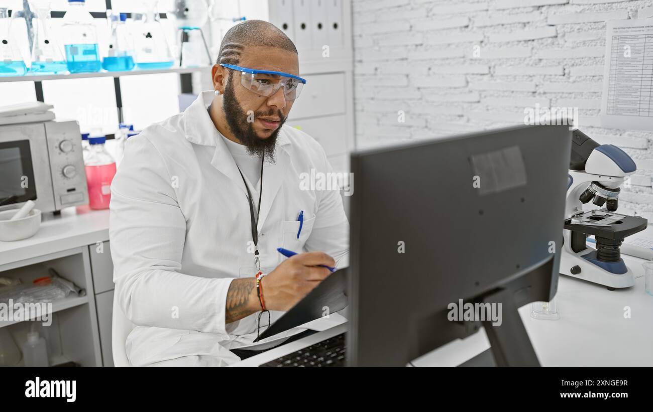 African man in lab coat taking notes at computer in modern laboratory ...