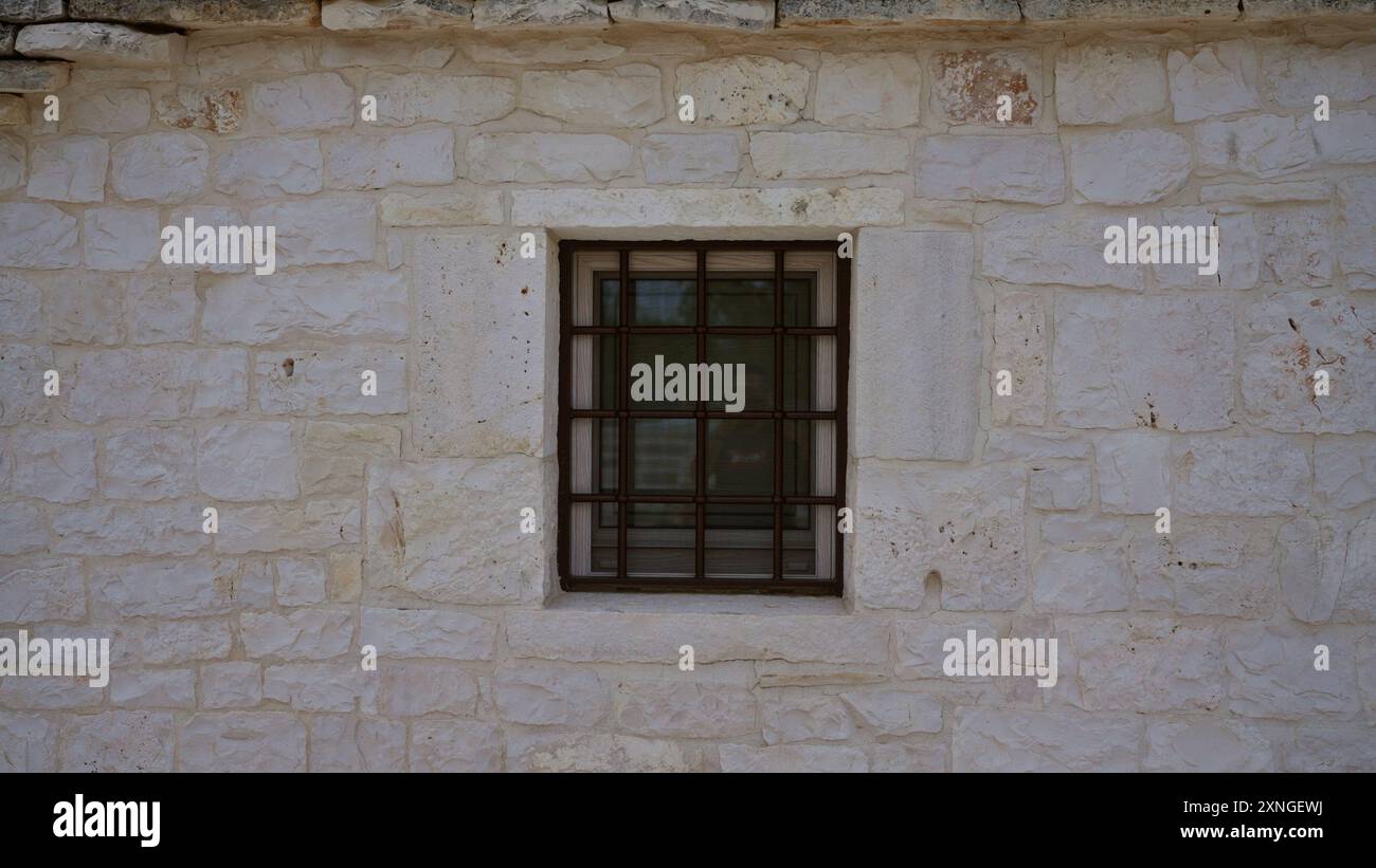A small, barred window set in a rustic, white stone wall of an outdoor ...