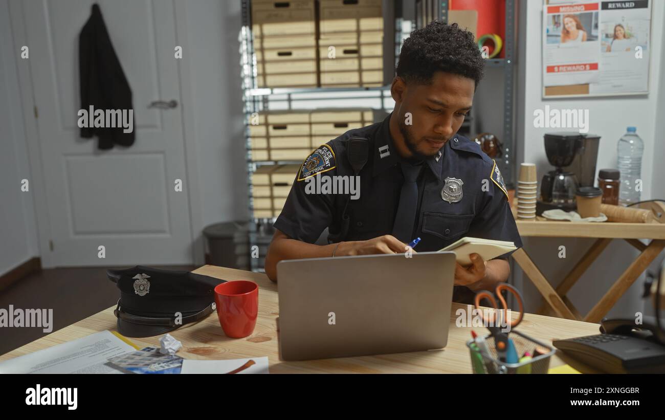 A focused african american male police officer takes notes at his desk ...