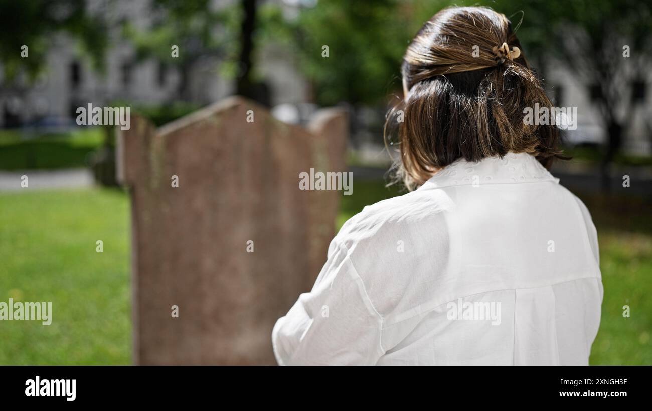 Beautiful young hispanic woman praying and mourning by tombstone at ...