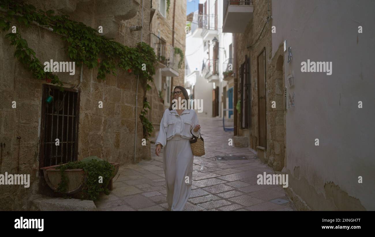A young hispanic woman walks through the charming streets of polignano ...