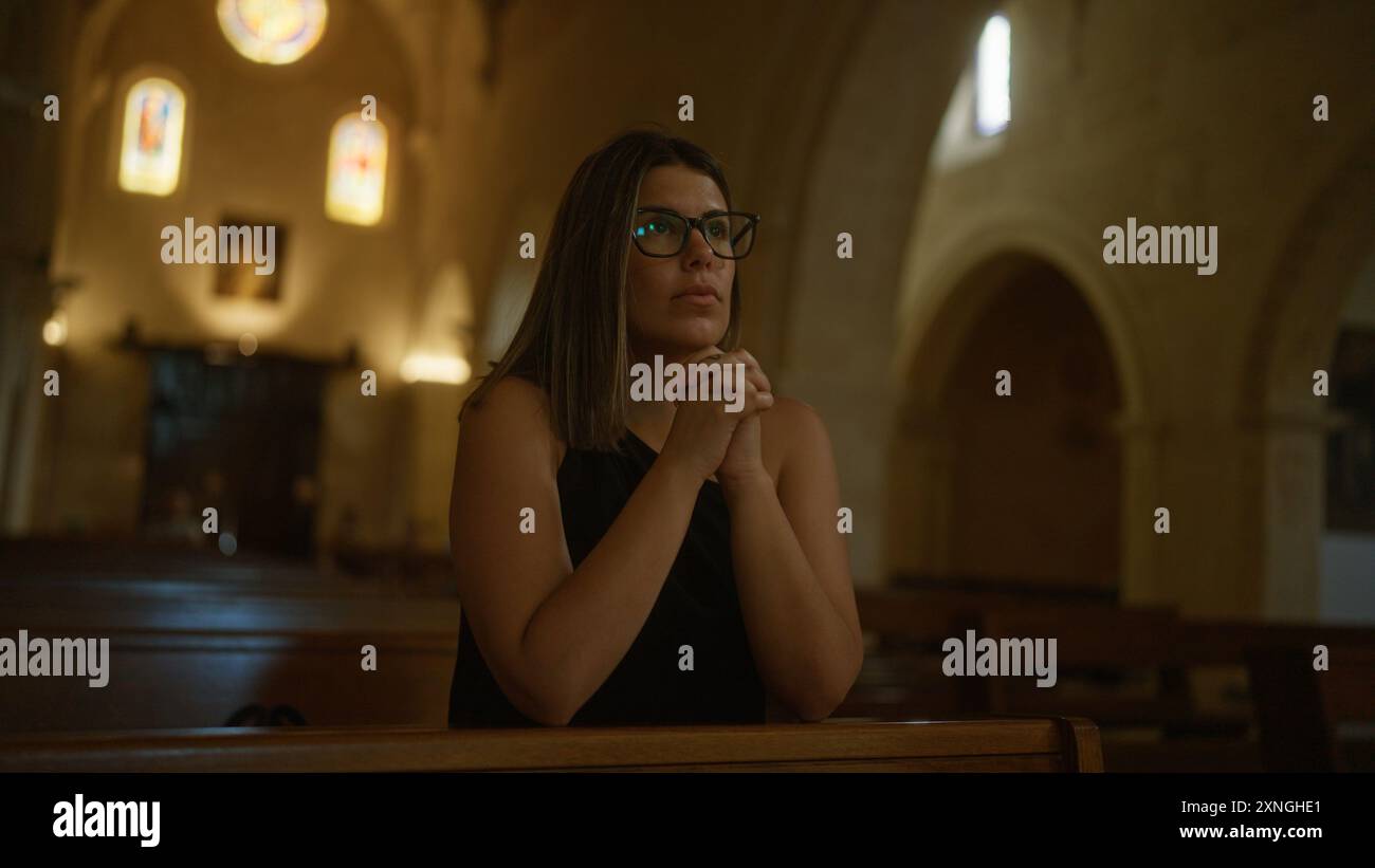 A young beautiful hispanic woman prays in a church in italy, surrounded ...