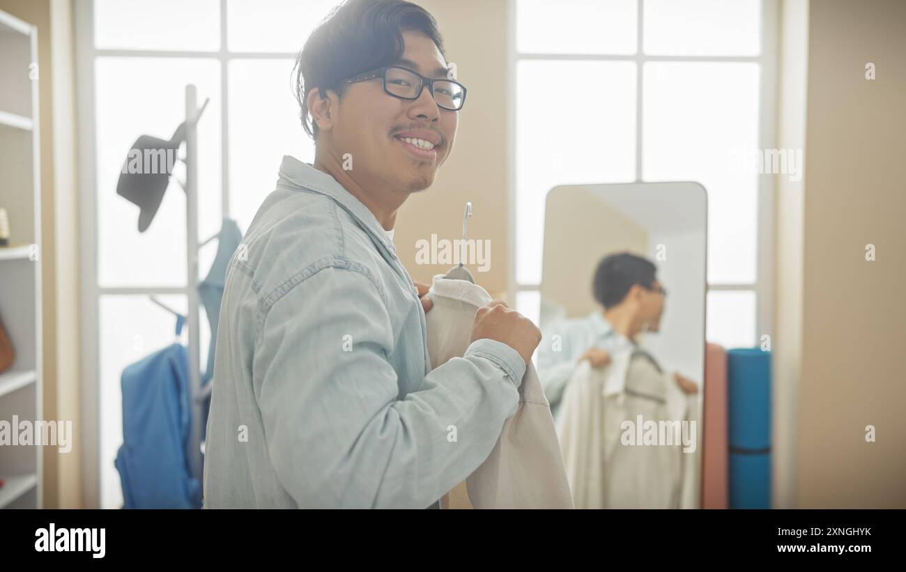 A smiling asian man trying on clothes in a well-lit dressing room ...