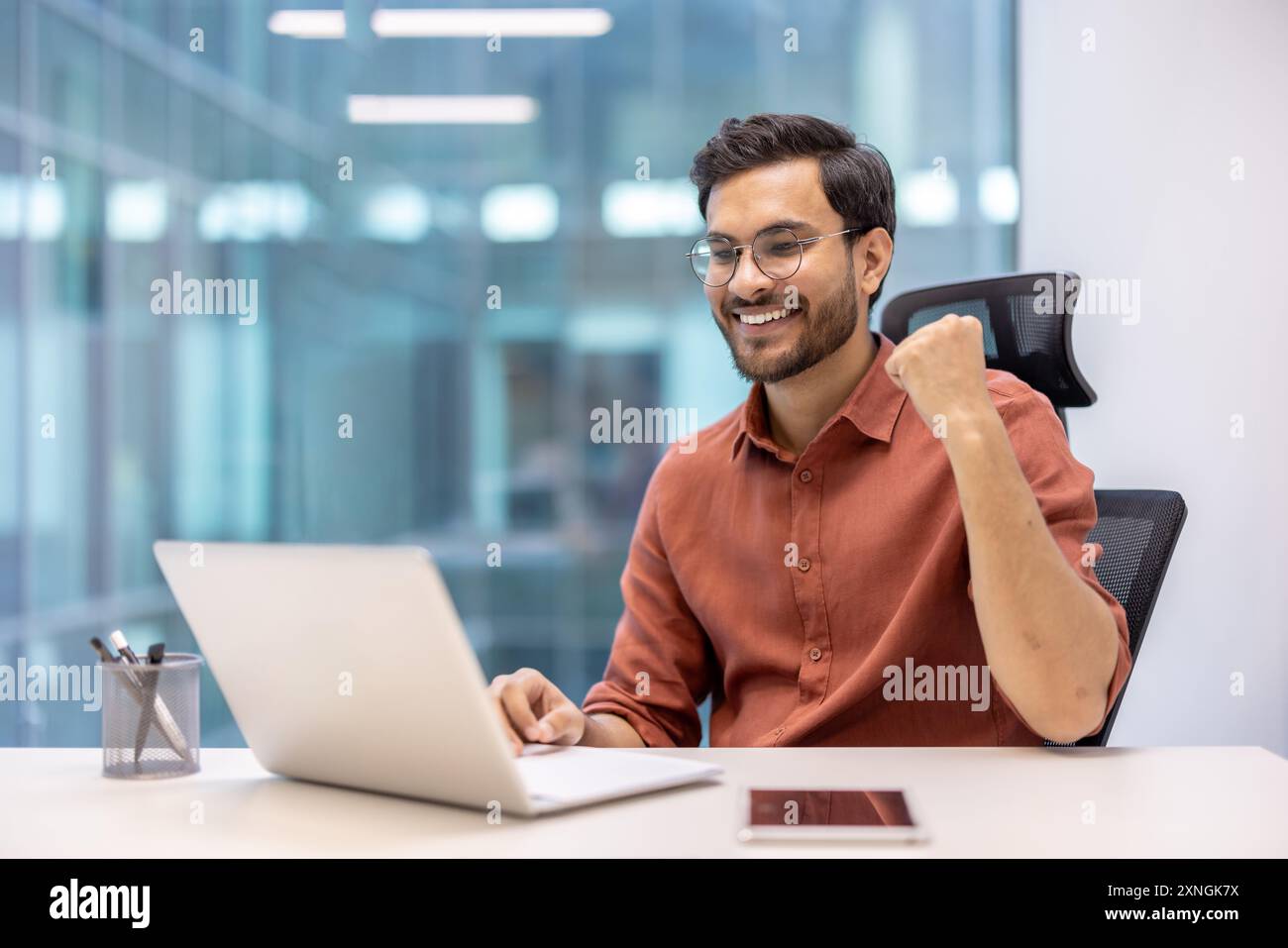 Smiling office worker in casual attire celebrating success at desk with ...