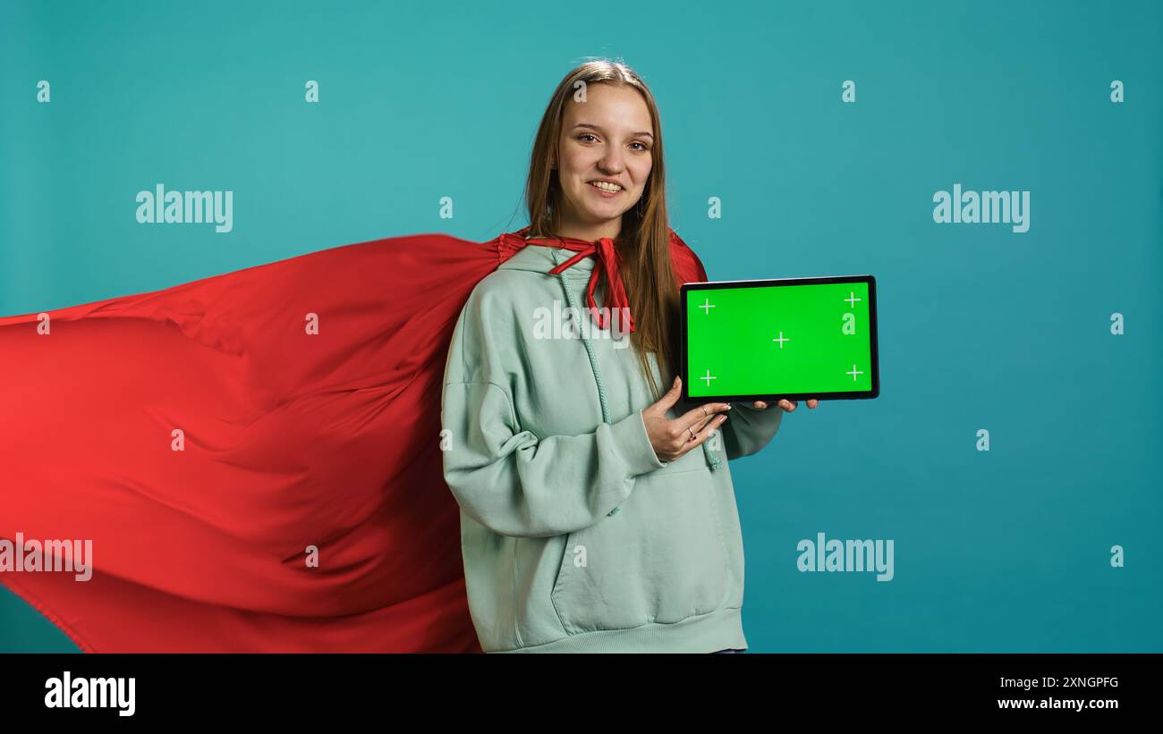 Joyous girl portraying superhero with red cape showcasing green screen ...