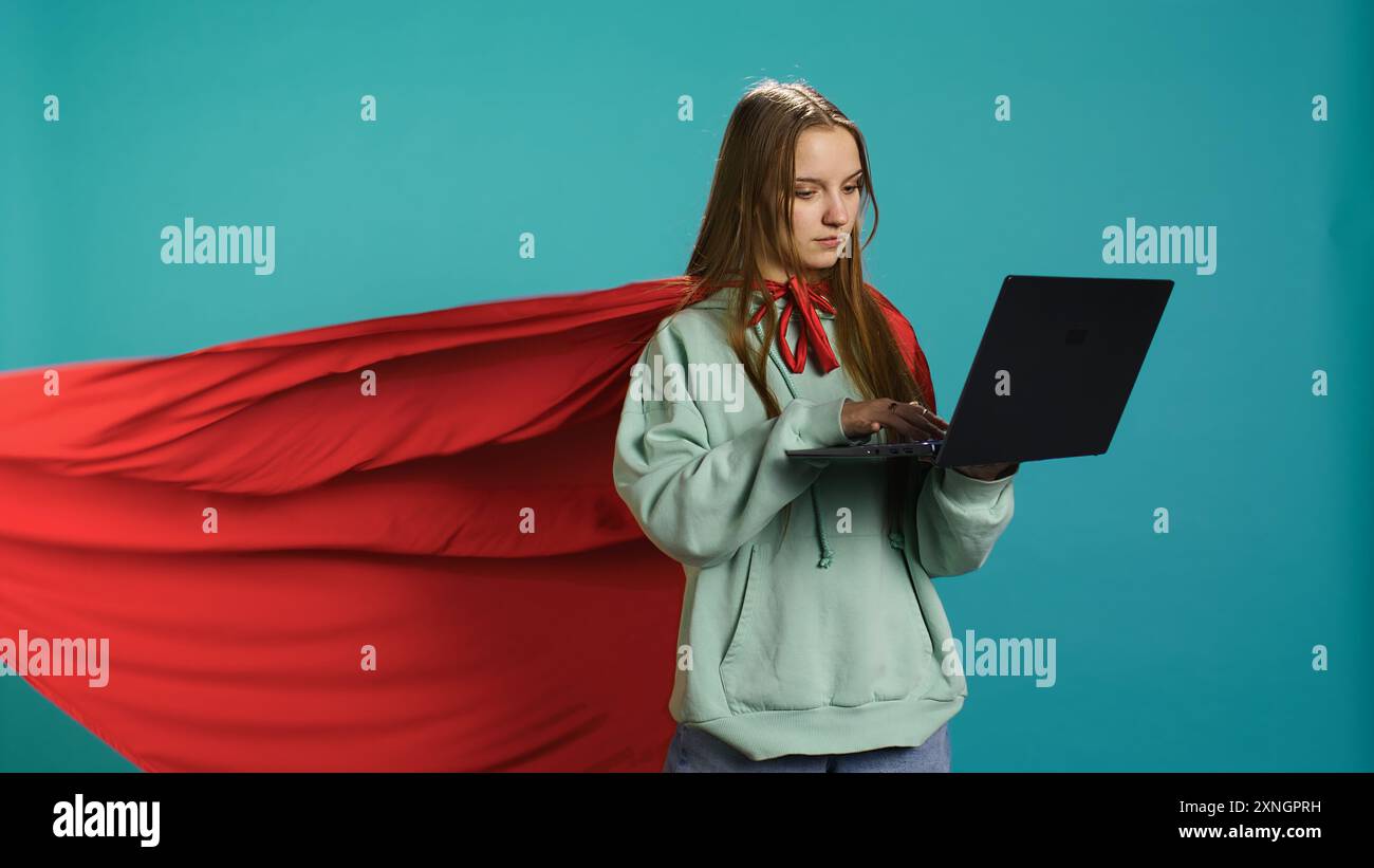 Young girl wearing superhero costume for Halloween working on laptop, isolated over studio ...