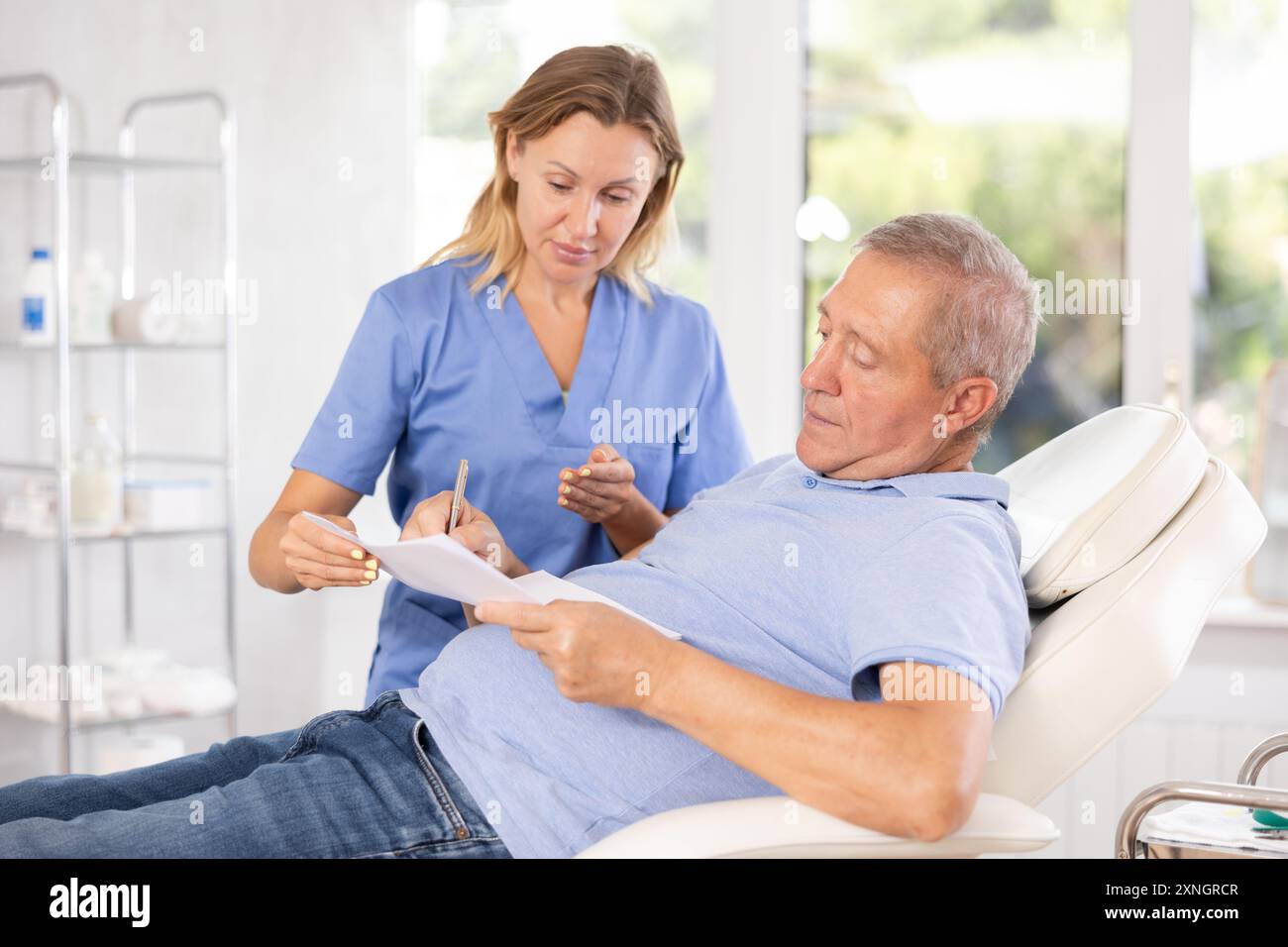 Old male patient signing papers while talking with woman doctor Stock ...