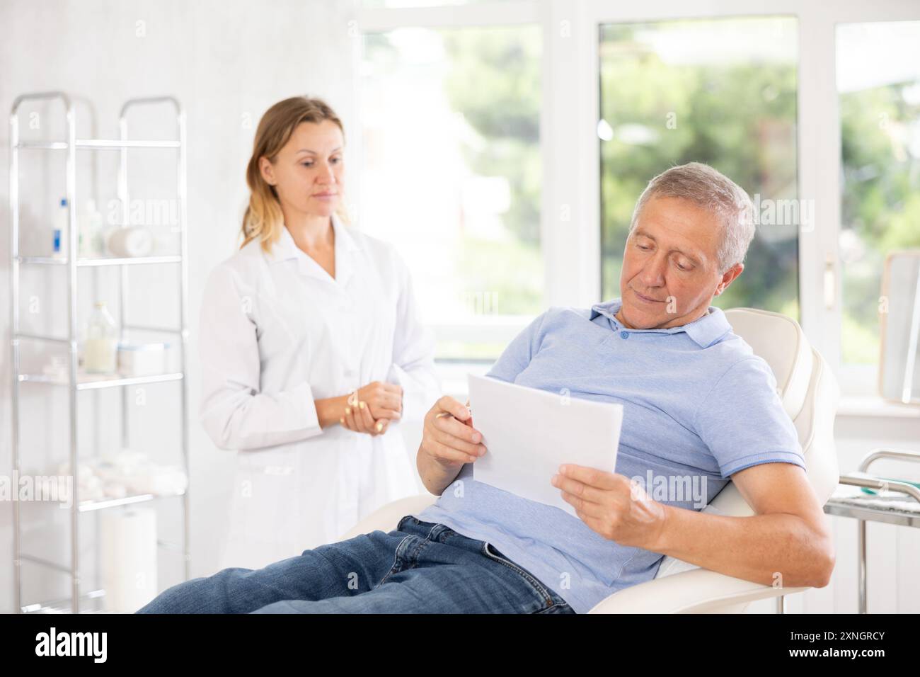 Old male patient signing papers while talking with woman doctor Stock ...