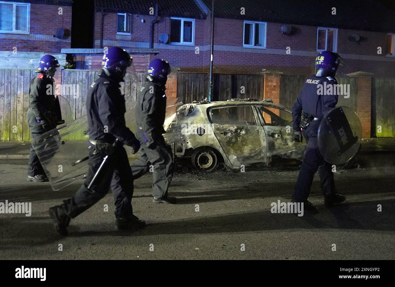 Police Officers walk past a burnt out police vehicle as they are ...