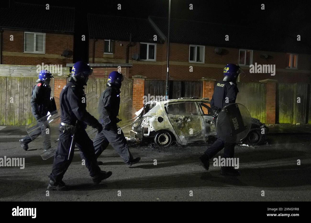 Police Officers walk past a burnt out police vehicle as they are ...
