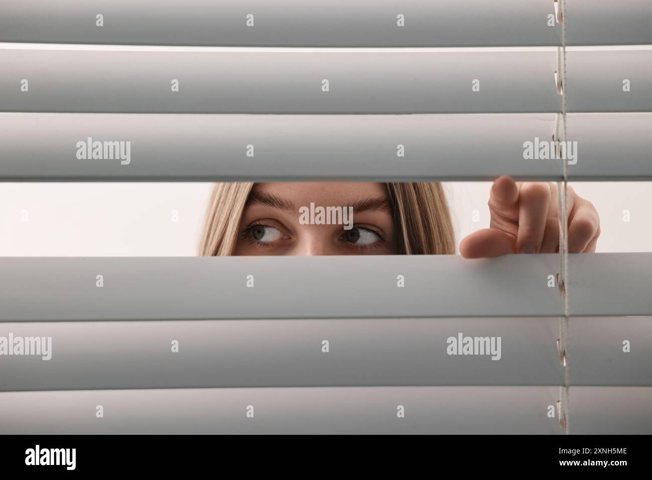 Young woman looking through window blinds on white background Stock ...