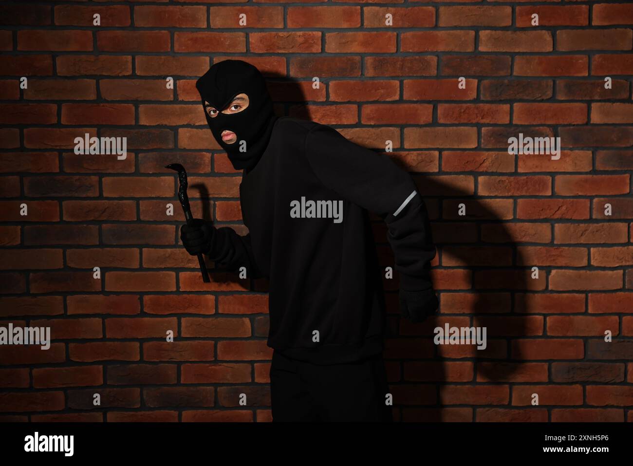 Thief in balaclava with crowbar against red brick wall Stock Photo - Alamy