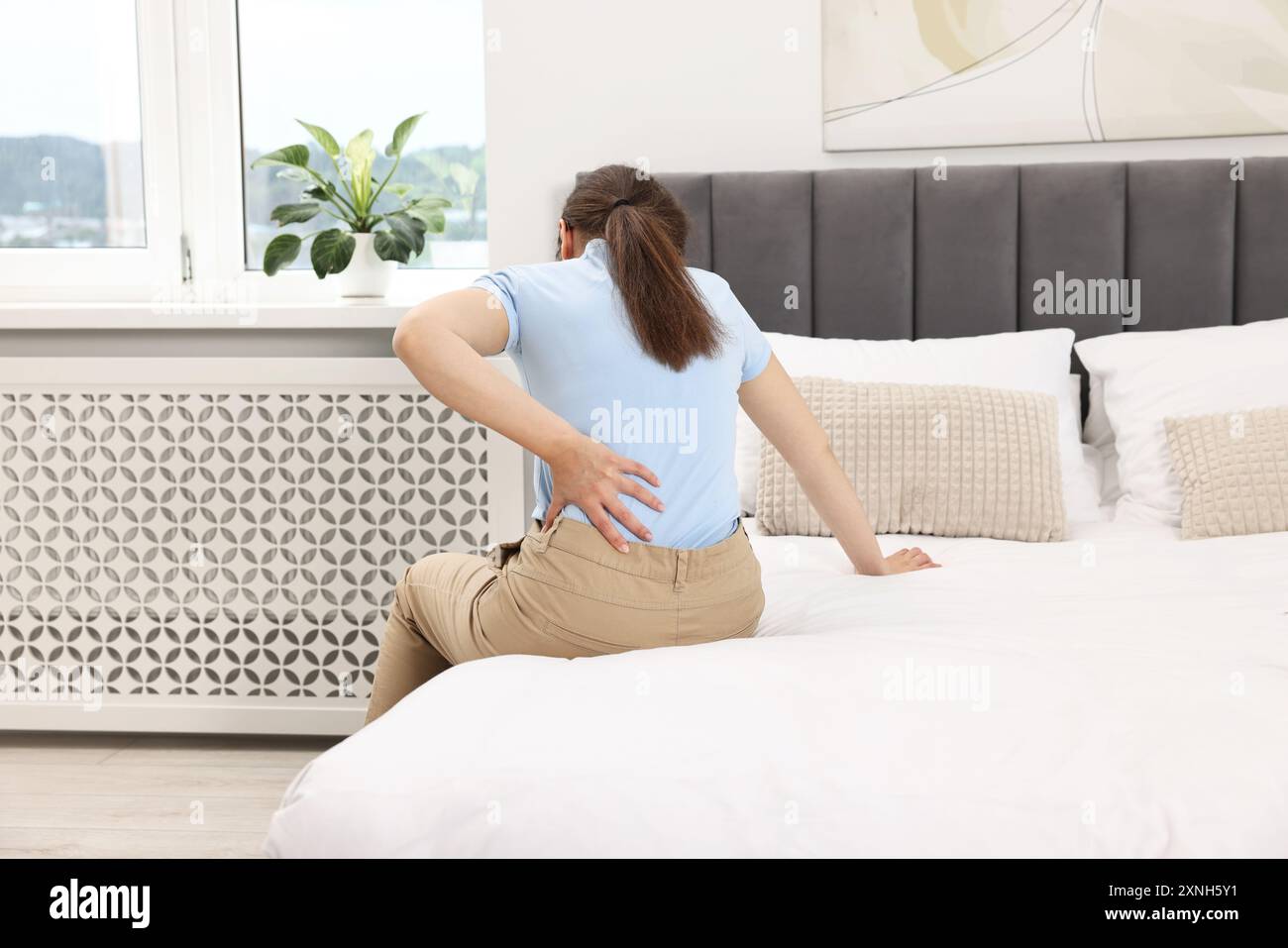 Woman suffering from back pain on bed at home, back view Stock Photo ...