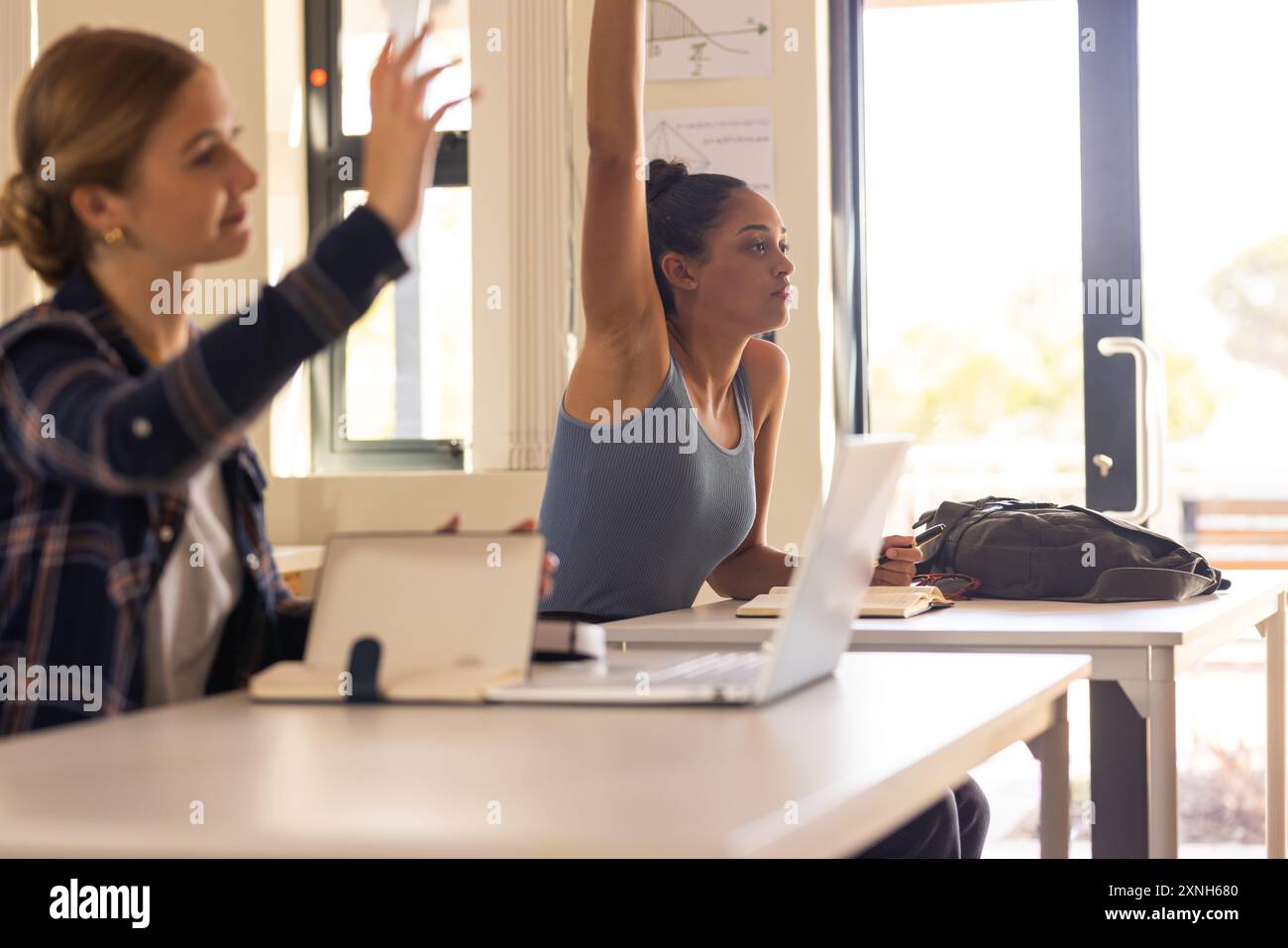 In high school, students raising hands in classroom with laptops and ...