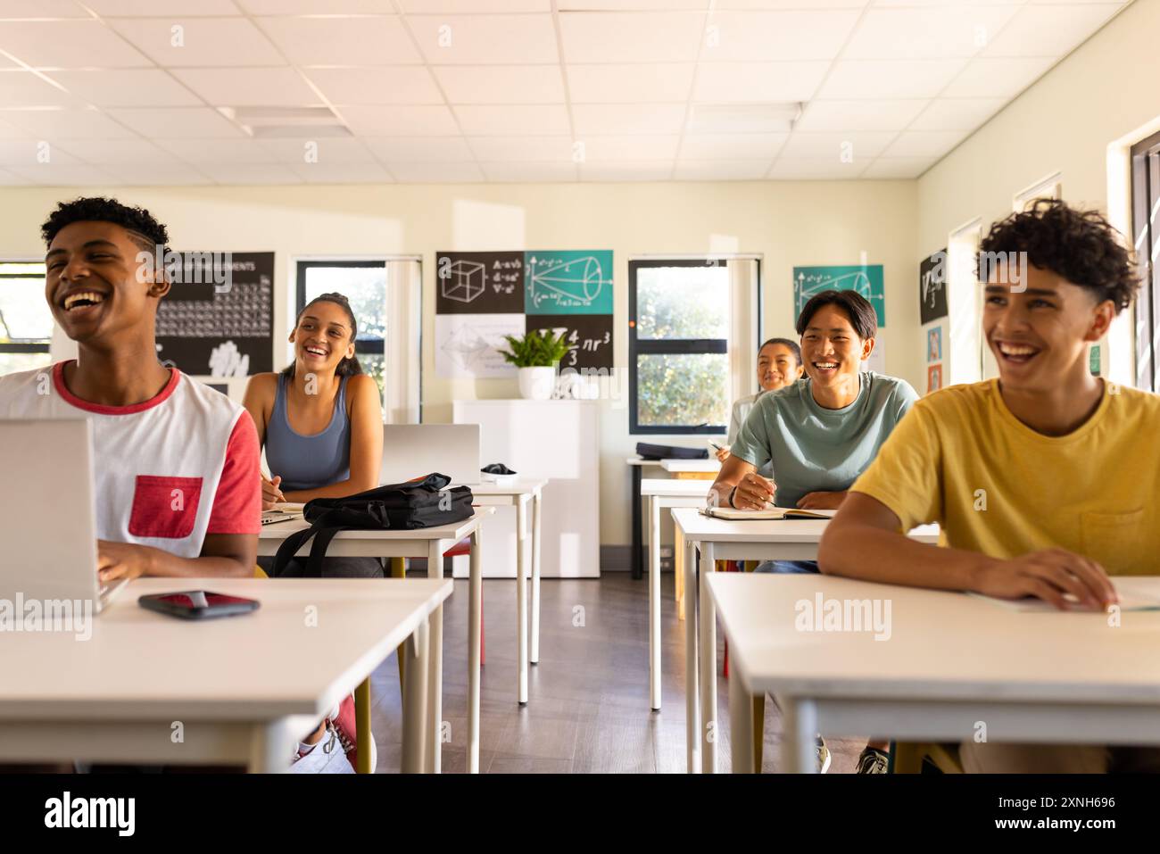 Teenagers in high school classroom, sitting at desks and smiling ...