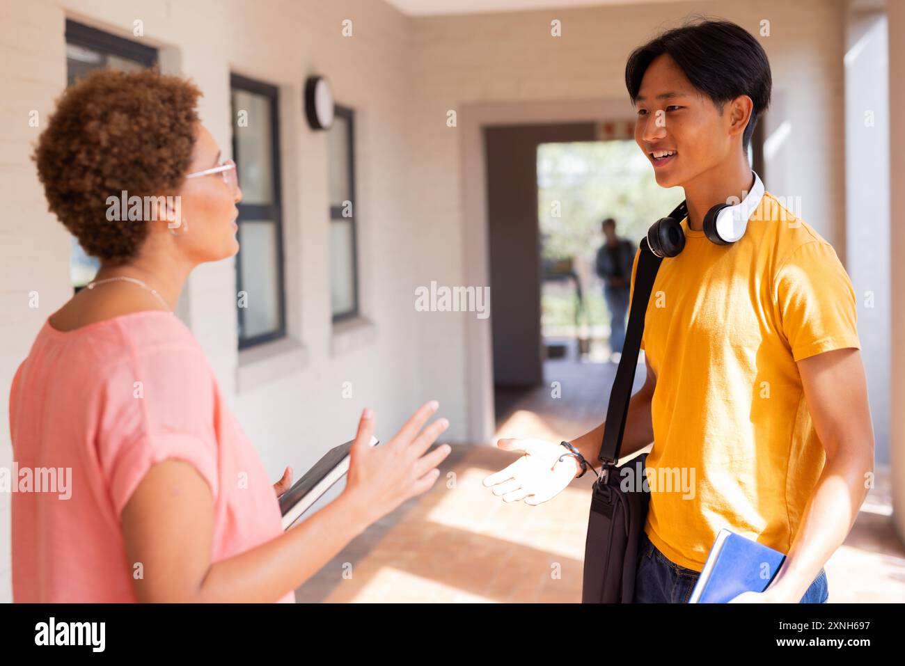 Talking in high school hallway, teenage boy with headphones and teacher ...