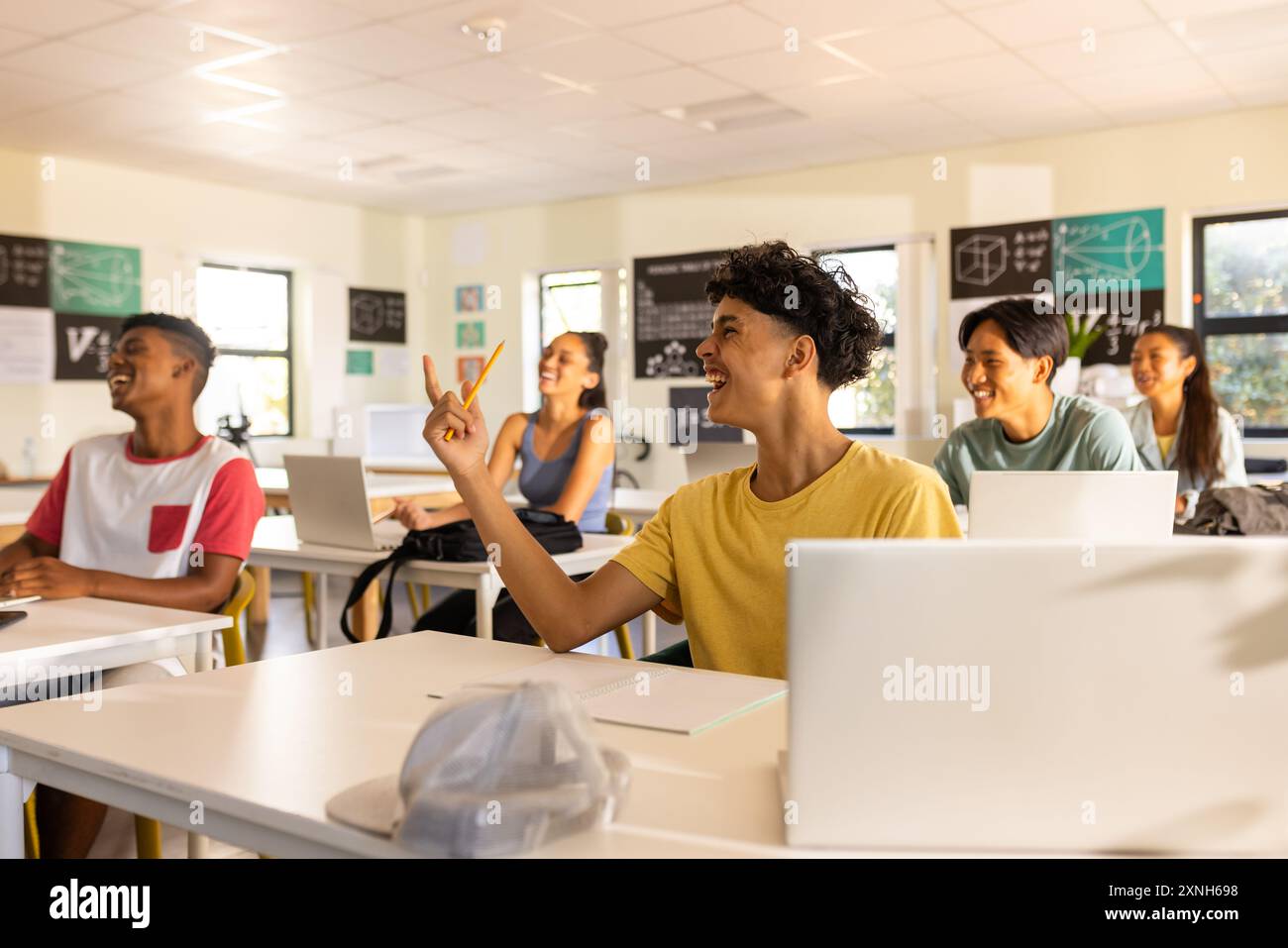 In high school, teenagers using laptops and raising hands in classroom ...