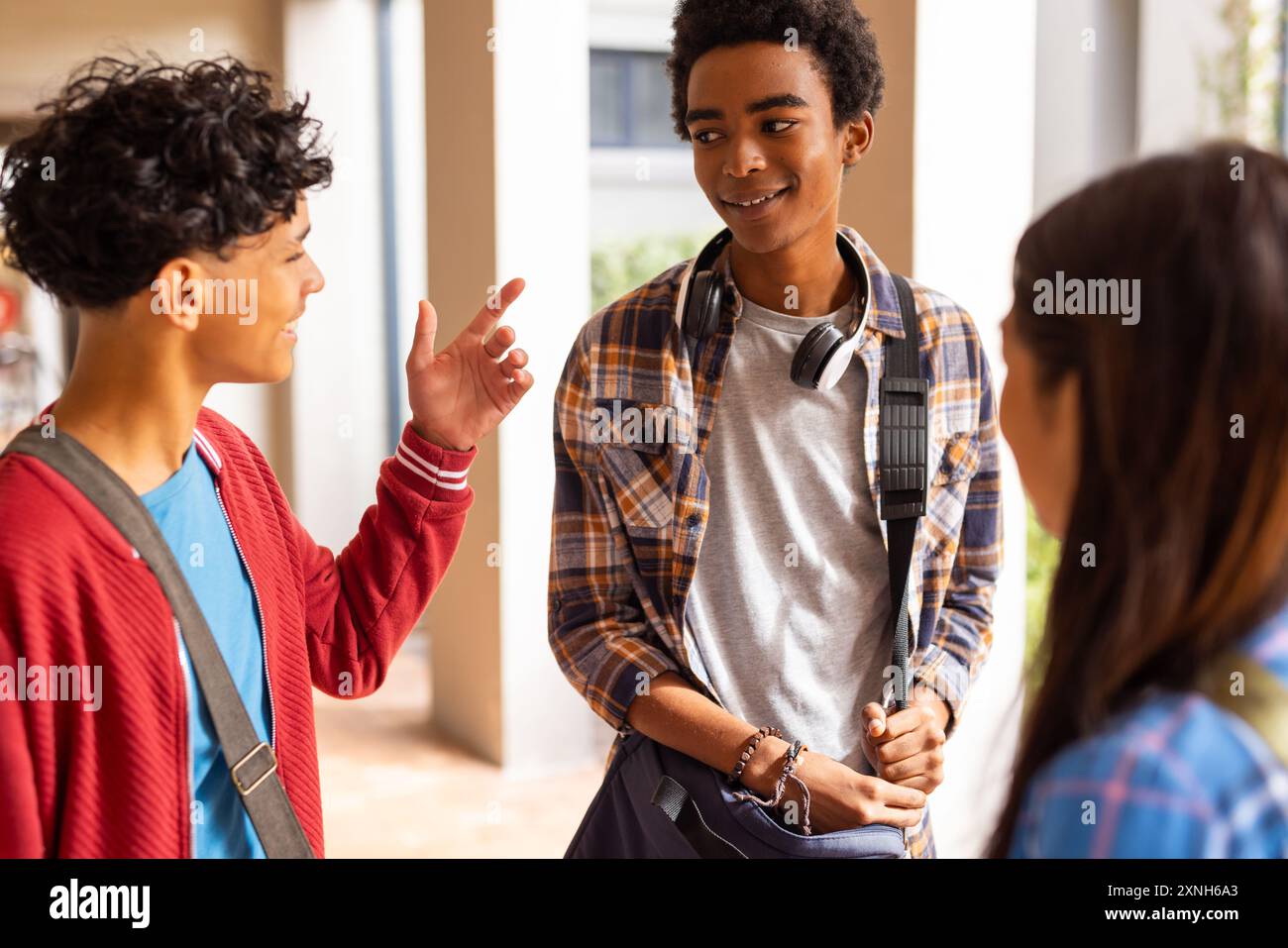 Teenagers talking and smiling, wearing backpacks and headphones at high ...