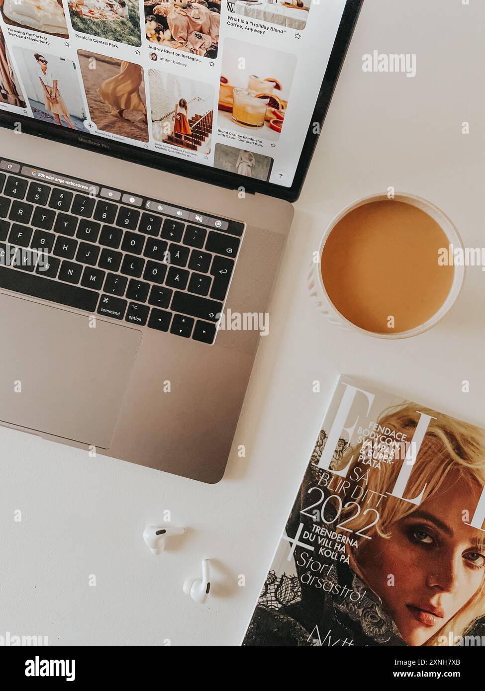 Workspace with a laptop, coffee, magazine, and earbuds on a white desk ...