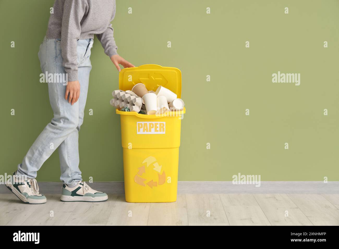 Woman putting garbage into full trash bin with PAPER sign near green ...