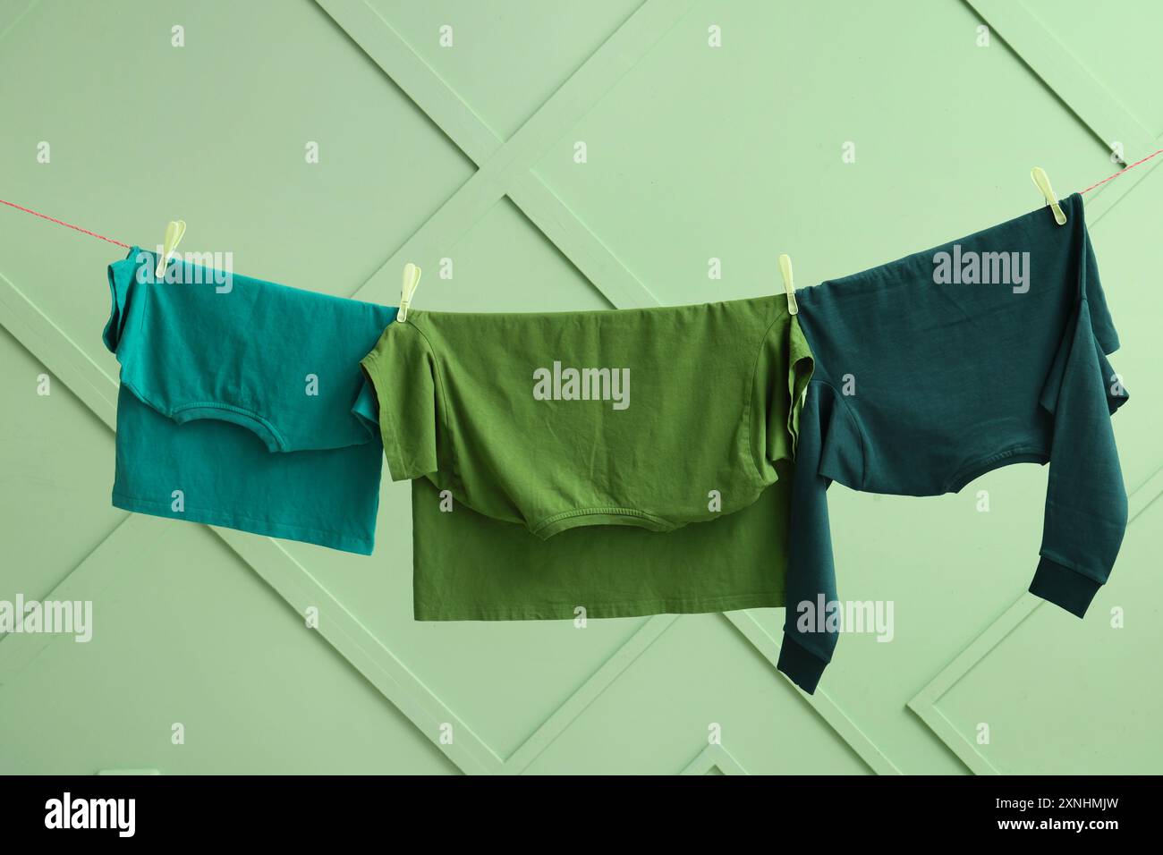 Clean clothes hanging on rope against color wall Stock Photo - Alamy