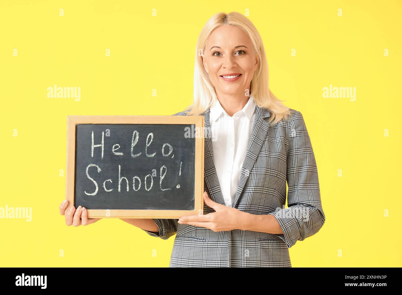 Mature female teacher holding chalkboard with text HELLO SCHOOL on ...