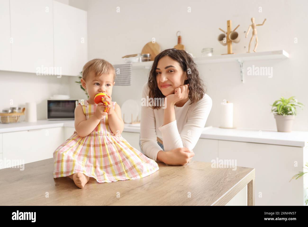 Cute little baby with nibbler eating food on table and mother in ...