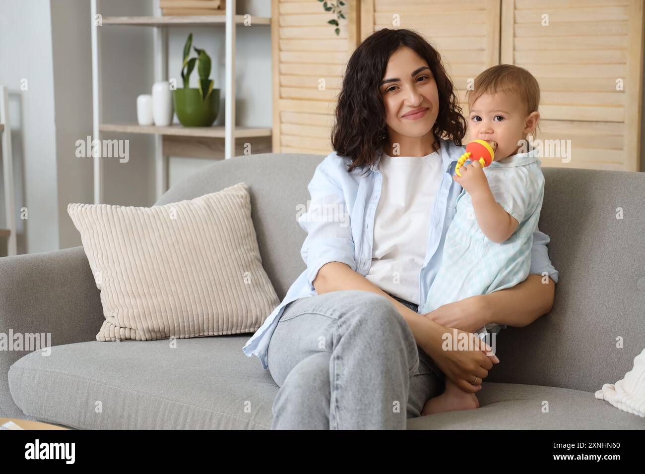 Mother and her little baby with nibbler eating food on sofa at home ...