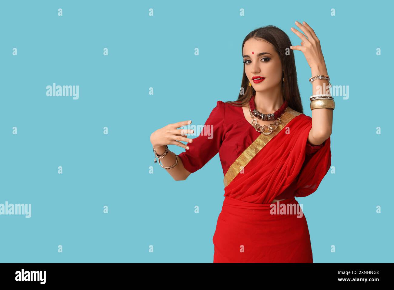 Beautiful young Indian woman in stylish sari dancing on blue background ...