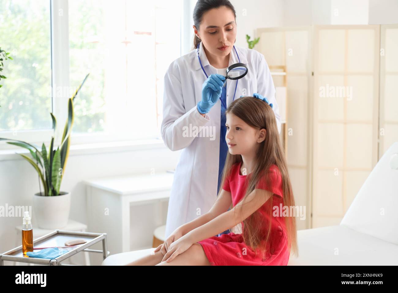 Female doctor with magnifier checking little girl's head for ...
