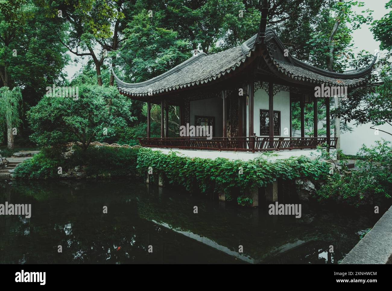 A traditional Chinese pavilion with a curved roof stands on stilts ...