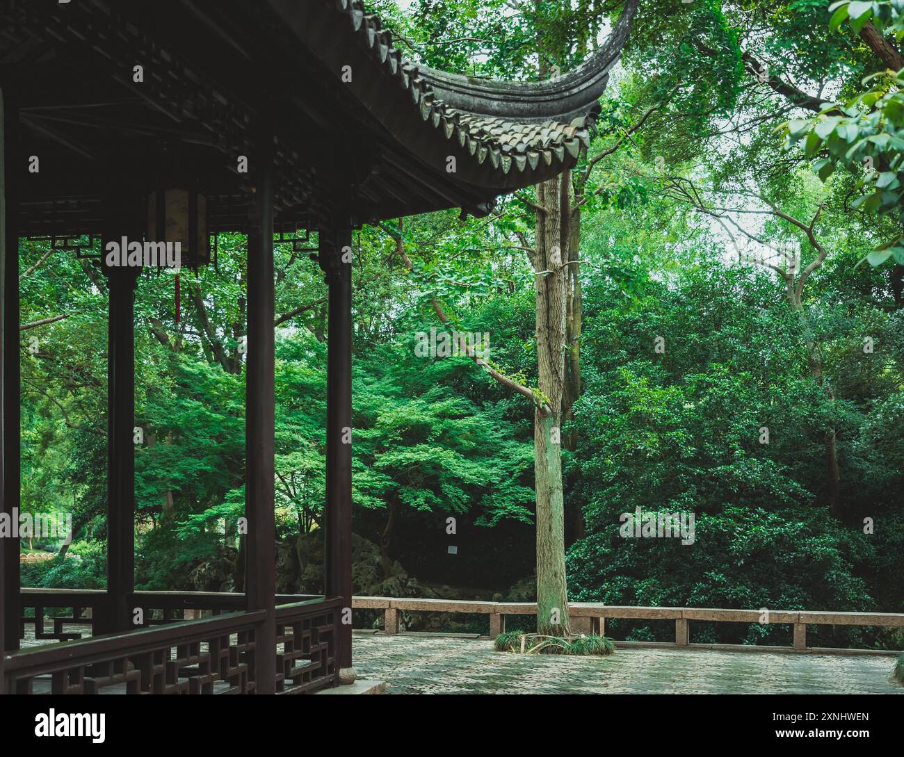 A traditional Chinese pavilion with a curved roof stands at the edge of ...
