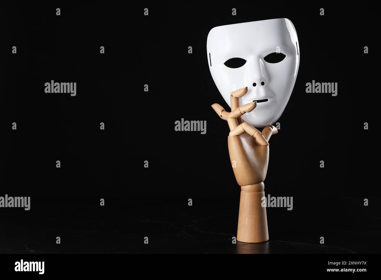Wooden mannequin hand holding plastic mask on black background, space ...
