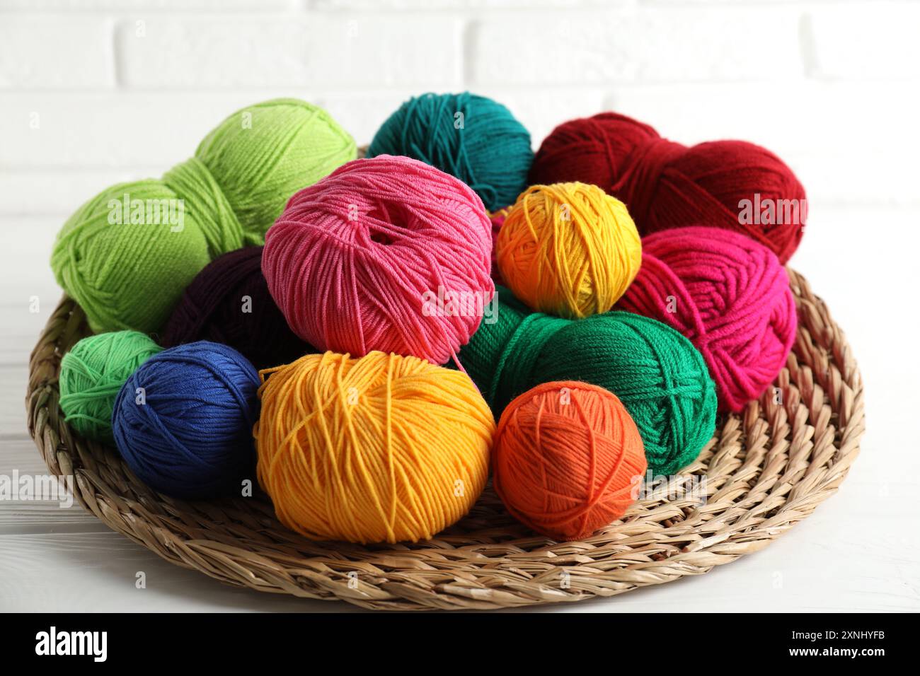 Pile of different yarns and wicker mat on white wooden table, closeup ...