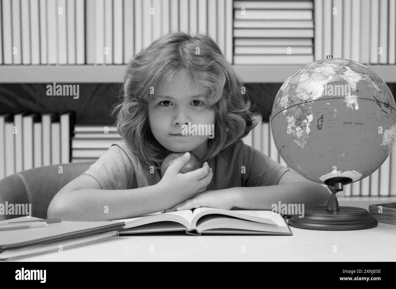 School boy with books and apple in library. Portrait of cute child ...