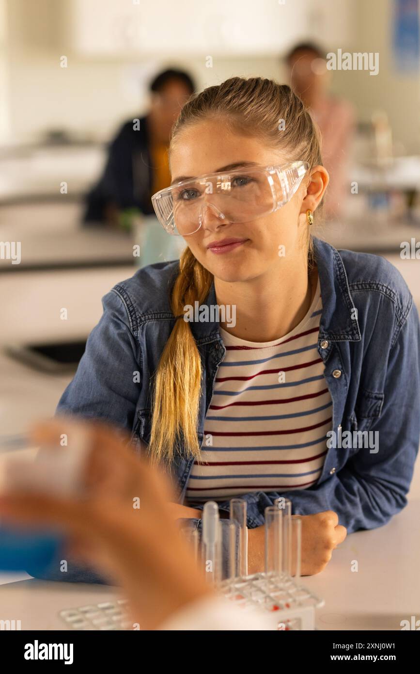 In high school, teenage girl wearing safety goggles observing science ...