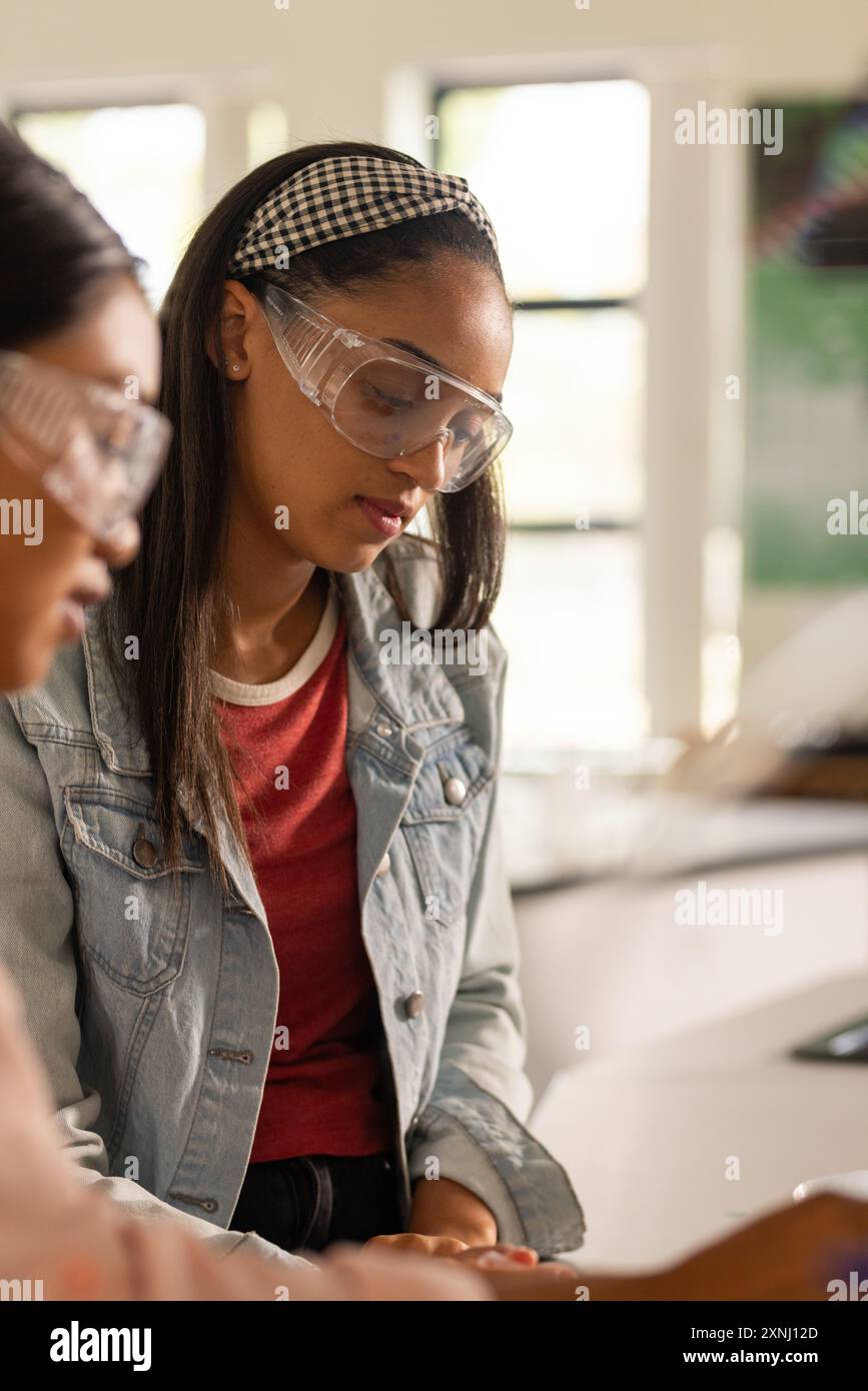 In high school, teenage girl wearing safety goggles focusing on science ...