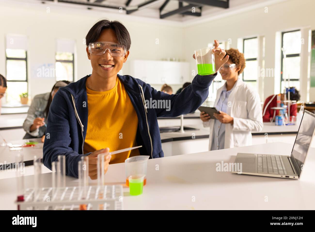 In high school laboratory, teenager holding beaker with green liquid ...