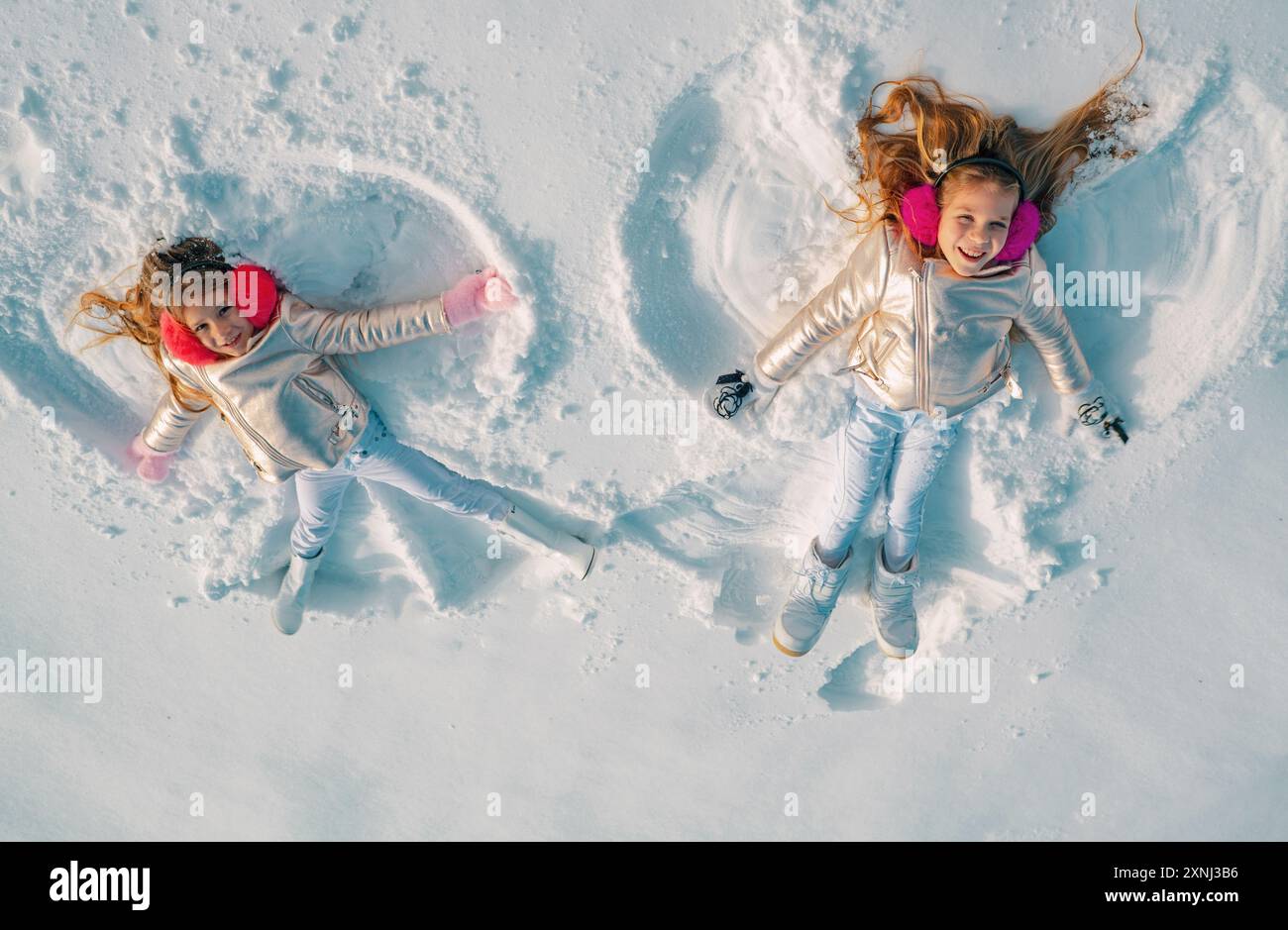 Two Girls on a snow angel shows. Smiling children lying on snow with ...