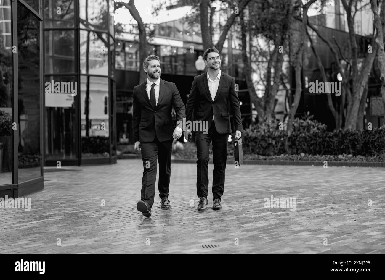Photo of businessmen in suits walking outdoor through city street. Two ...