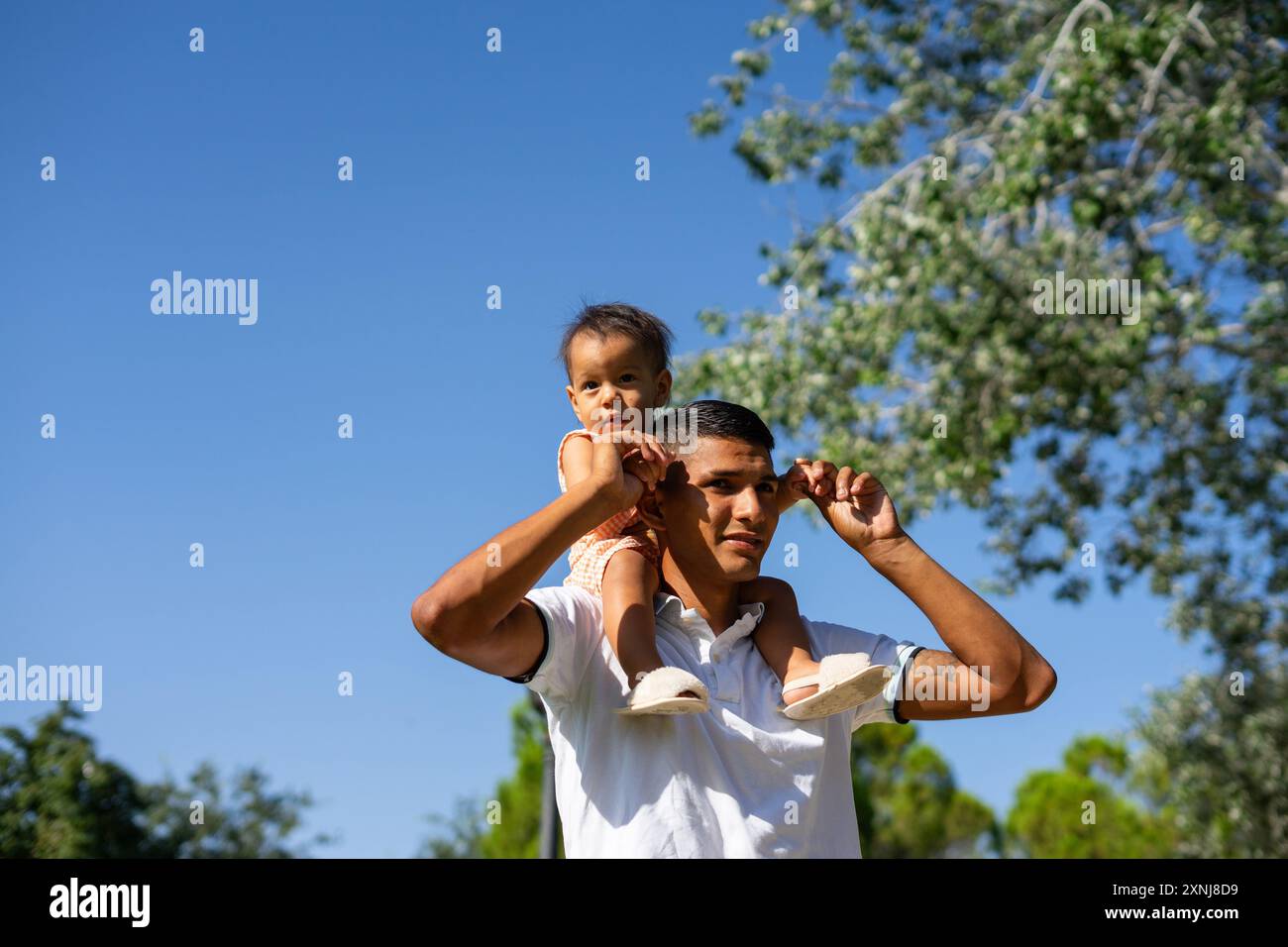 Baby girl standing on her father's shoulders outdoors. Peruvian family ...