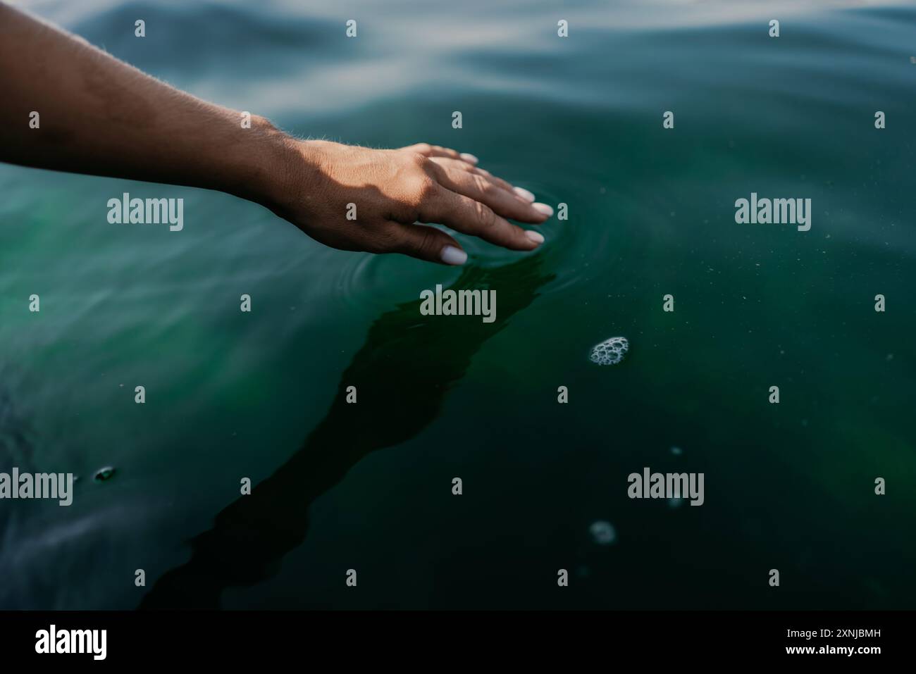 The hand touches the water, creating ripples. The water is calm and ...