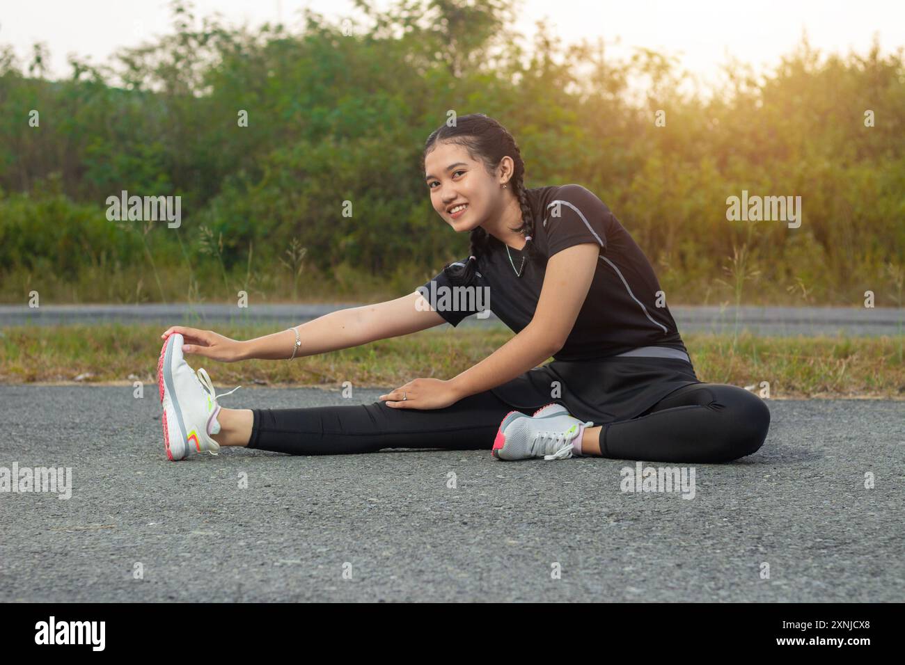 Beautiful Asian sports girl in black suit sitting in park doing warm up ...