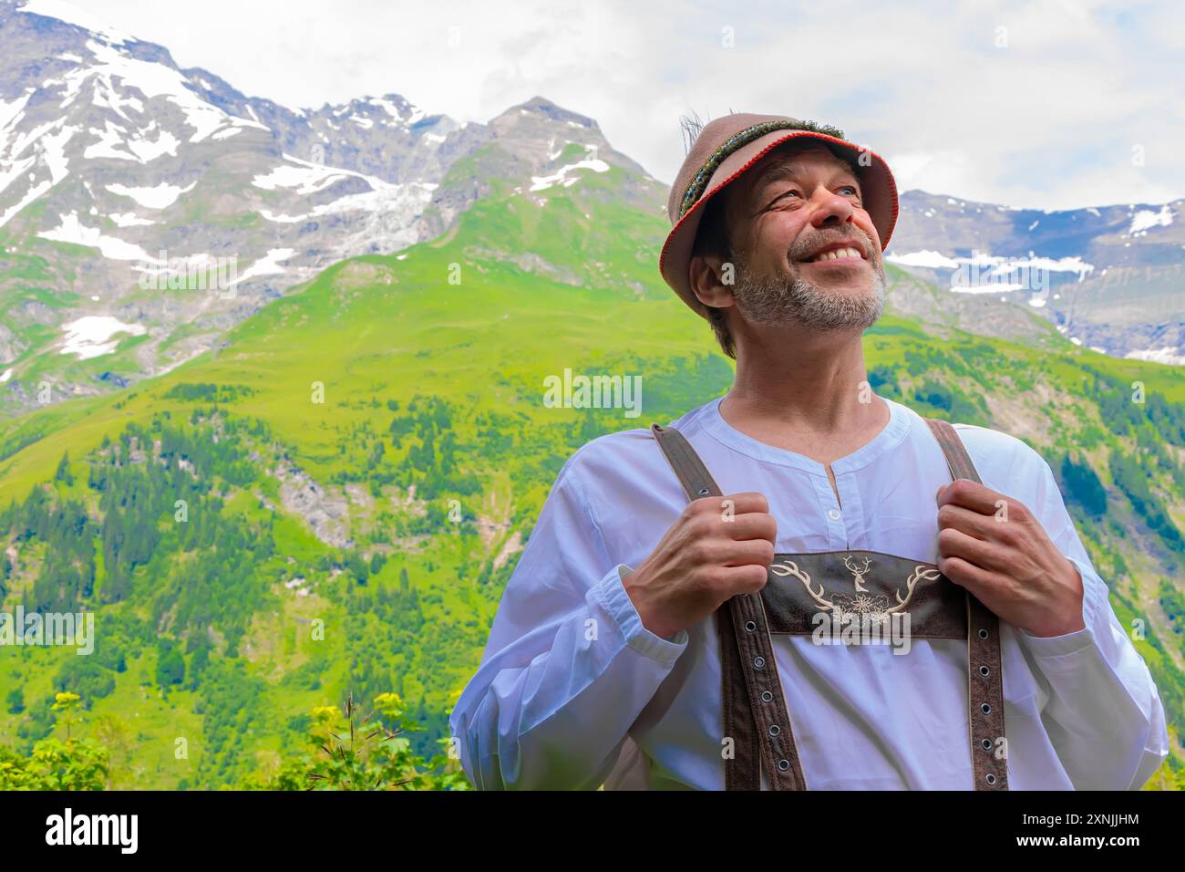 An elderly man in traditional Alpine garb stands on a mountain ridge ...